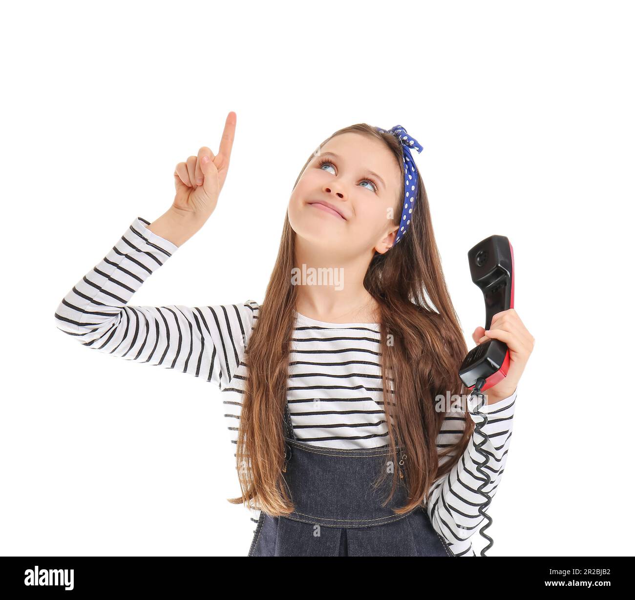 Little girl with phone receiver pointing at something on white ...