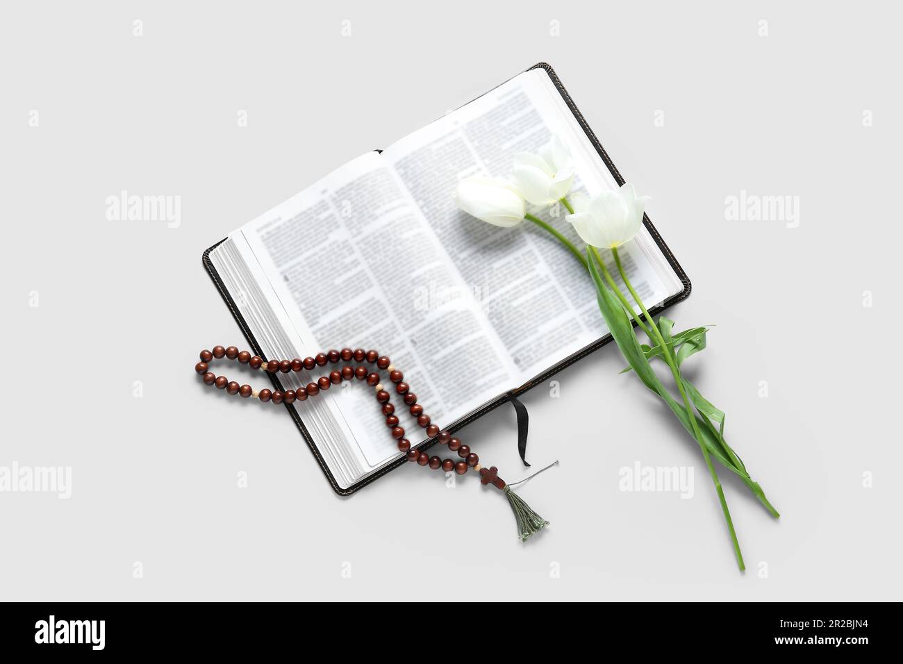 Open Holy Bible with prayer beads and tulip flowers on pale blue ...