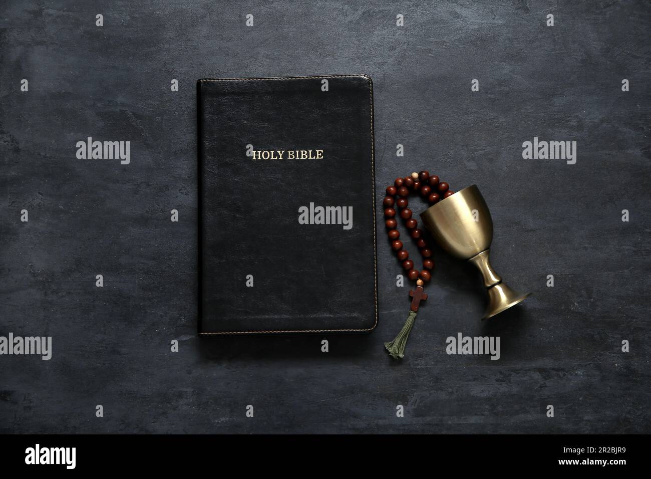 Holy Bible with prayer beads and chalice on grunge black background ...