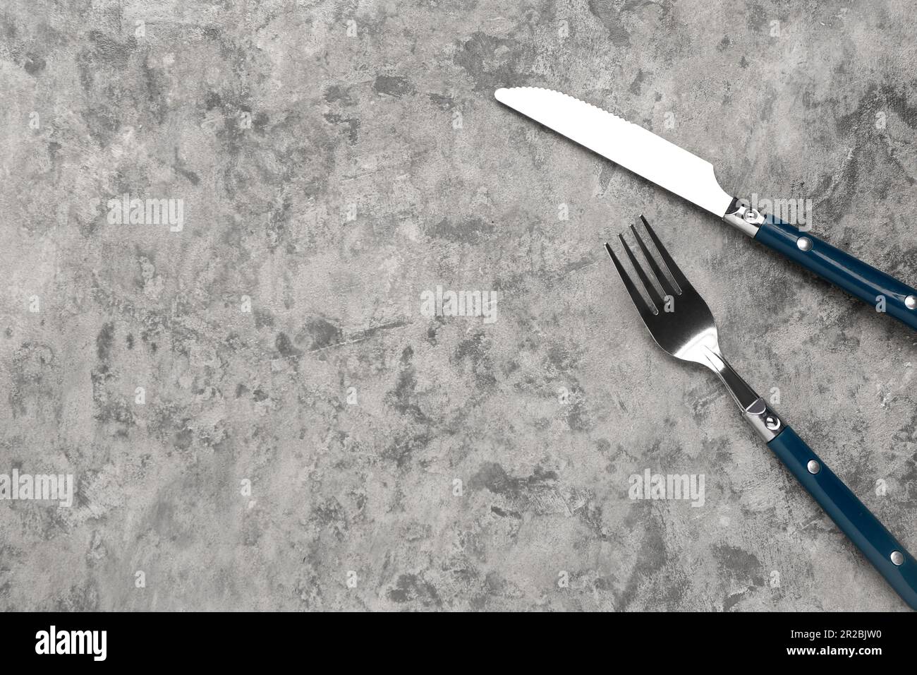 Stainless steel fork and knife with blue handles on grey background ...