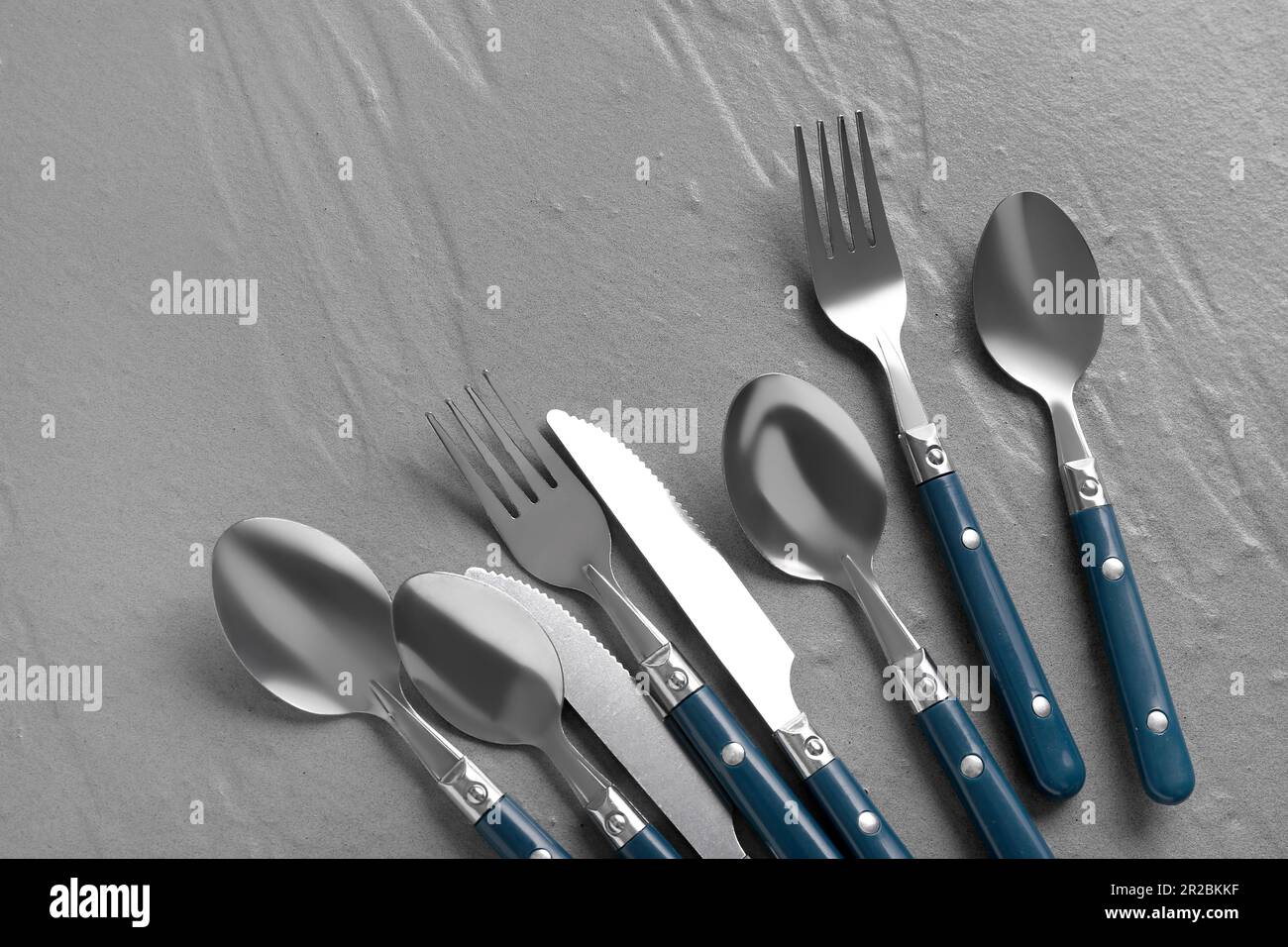 Stainless steel set of cutlery with blue handles on grey background ...
