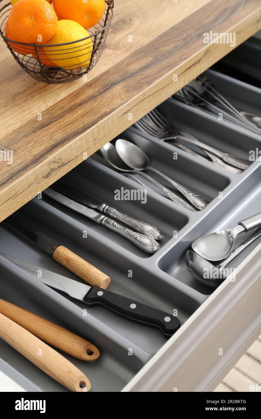 Open kitchen drawer with different silver cutlery and bowl of fruits ...