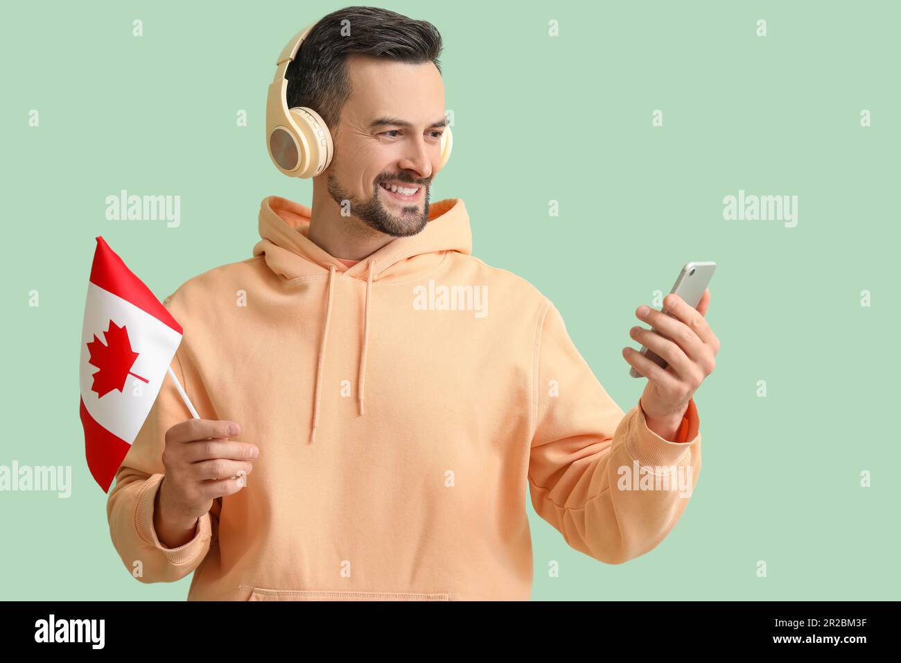 Handsome man in headphones with flag of Canada and mobile phone on ...