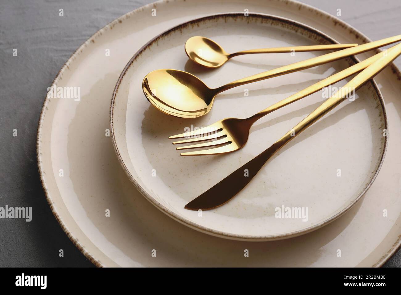 Golden set of cutlery with beige plates on grey background Stock Photo ...