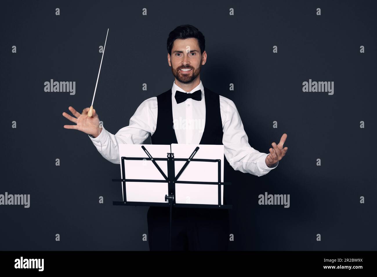 Happy professional conductor with baton and note stand on grey ...
