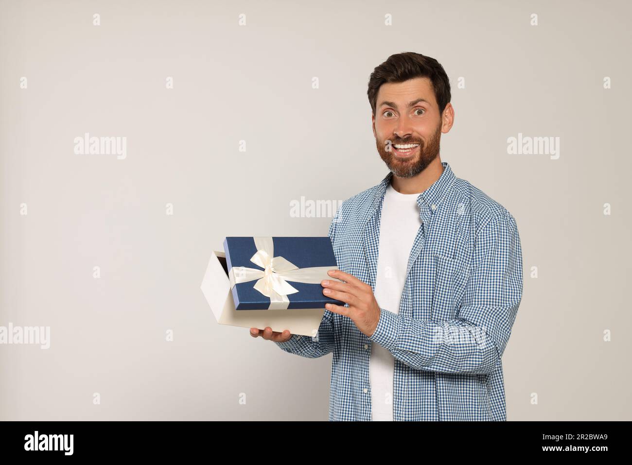 Emotional man opening gift box on light grey background, space for text ...