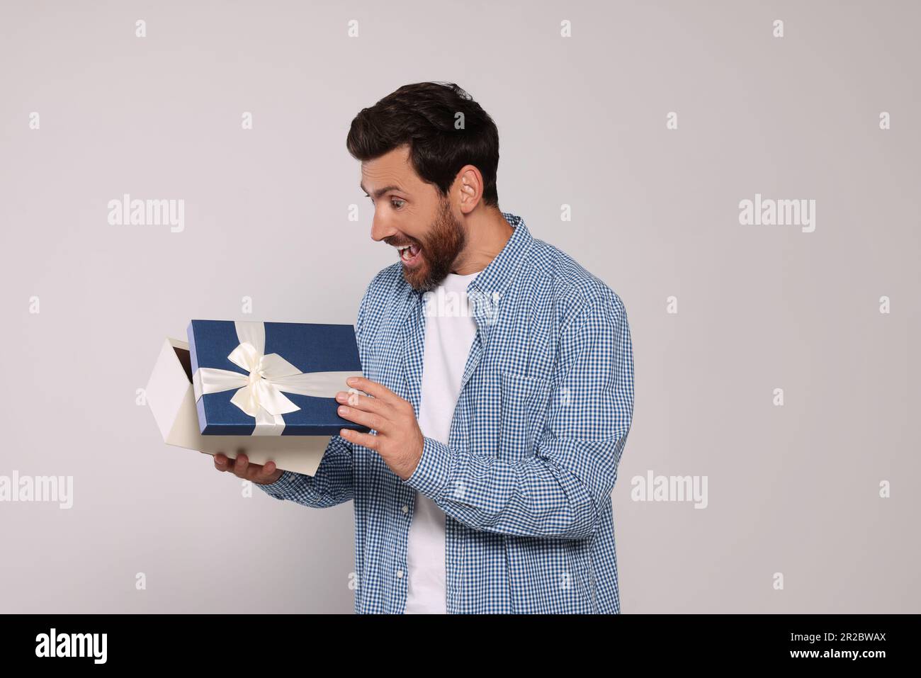 Emotional man opening gift box on light grey background Stock Photo - Alamy