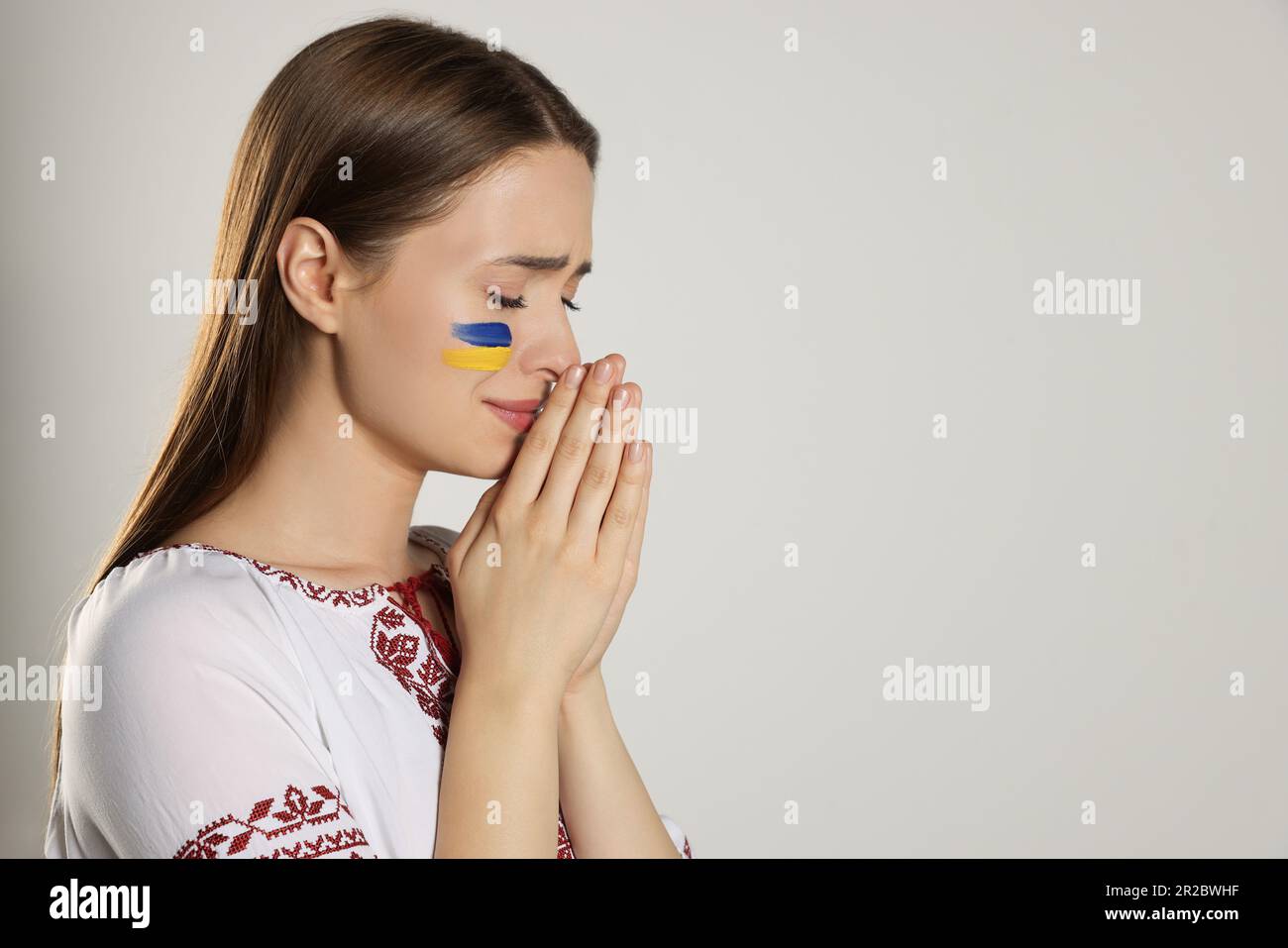 Sad young Ukrainian woman with clasped hands on beige background, space ...