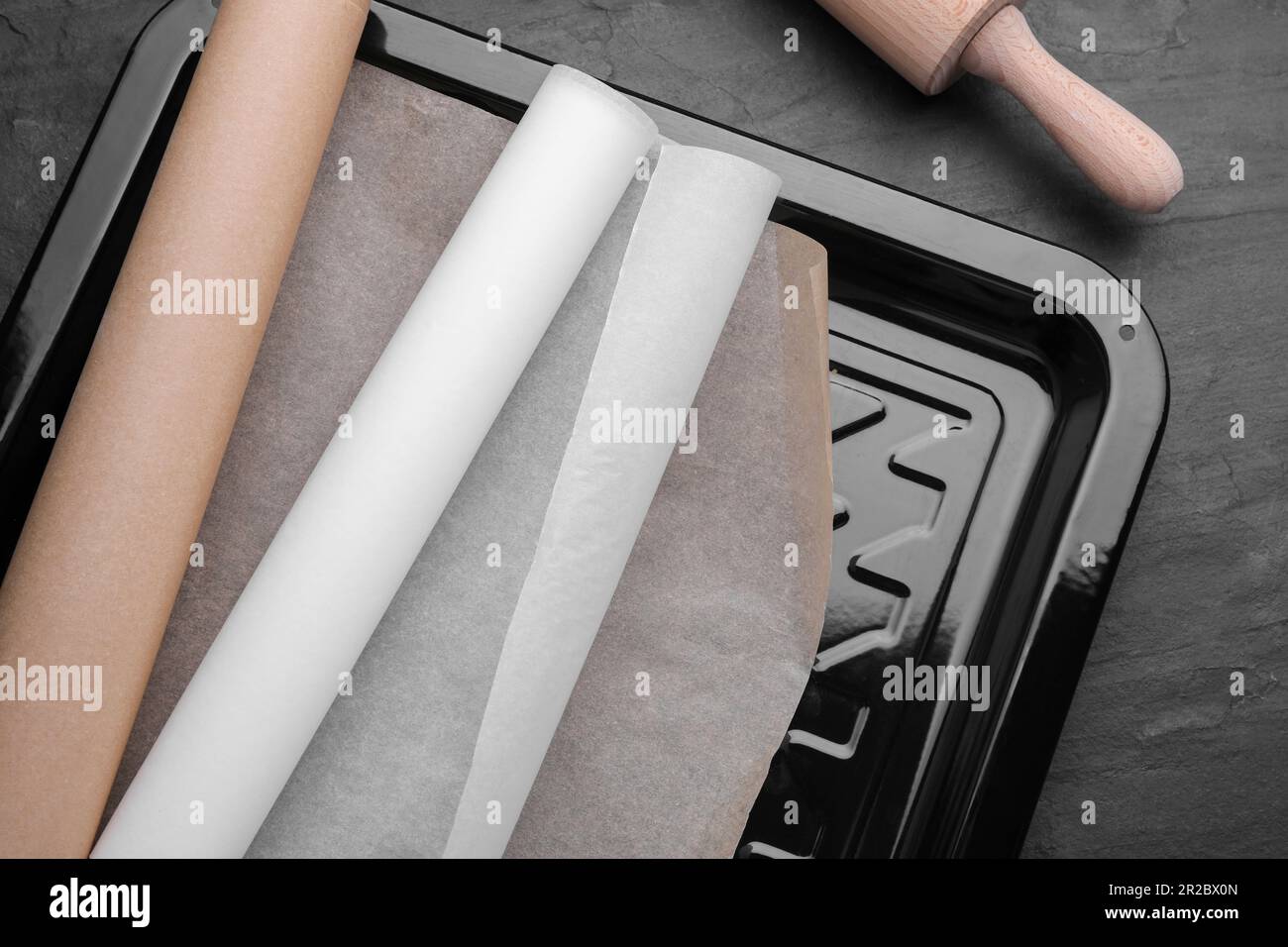 Baking pan with rolls of parchment paper on black table, top view Stock ...