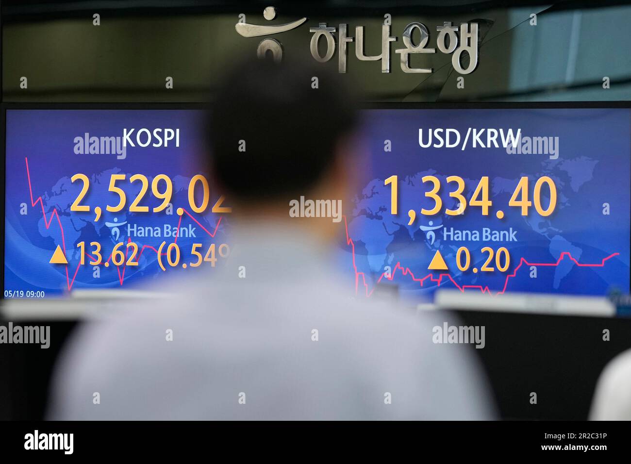 A currency trader walks by the screens showing the Korea Composite Stock Price Index (KOSPI ...
