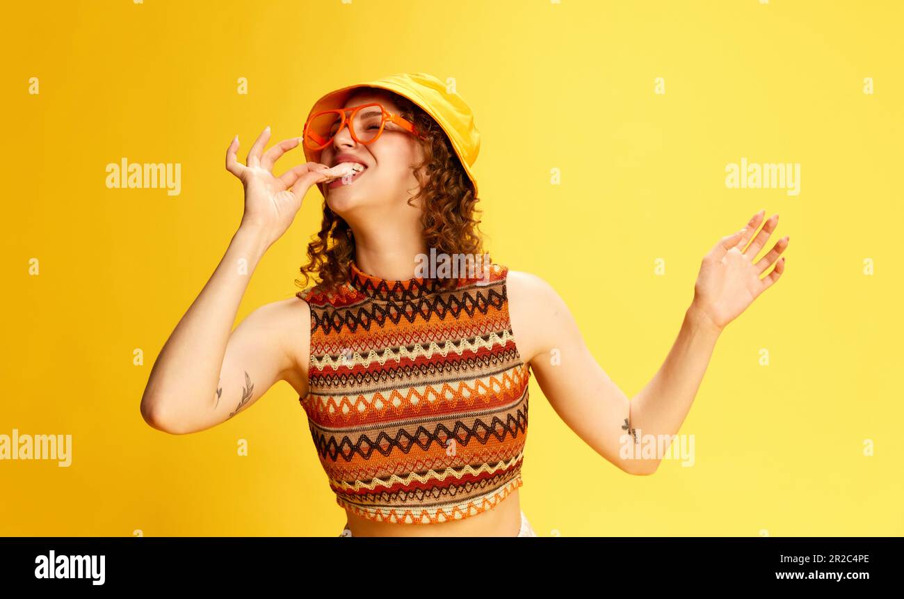 Portrait of pretty young girl in panama and knitted top eating candy ...