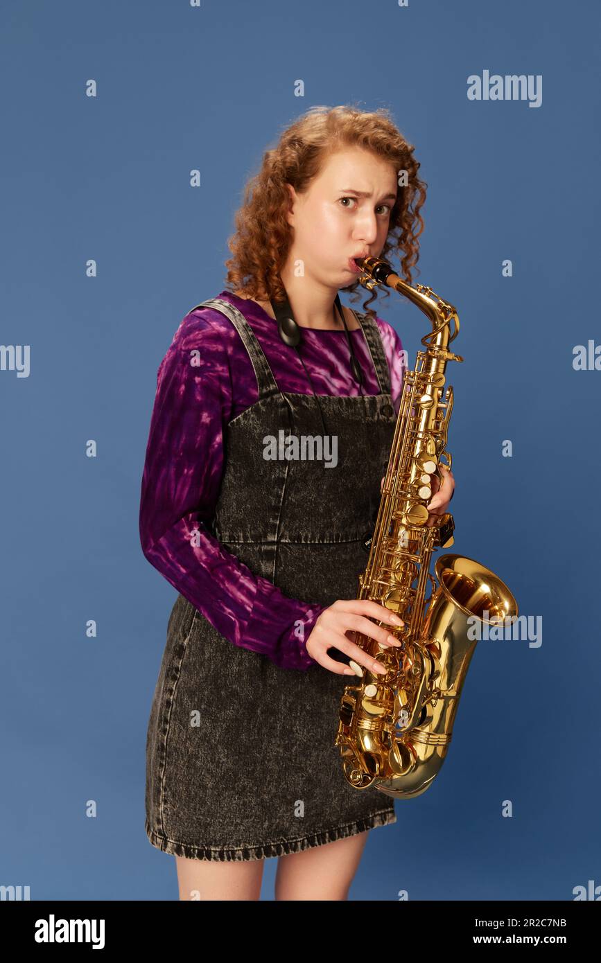 Portrait of emotional young girl in dress playing saxophone against ...