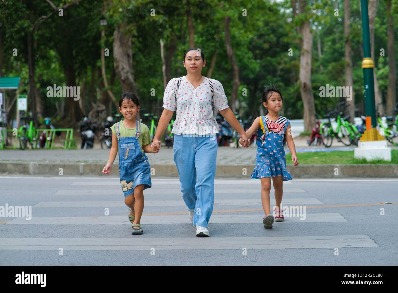 Mother and children holding hands cross the road on the crosswalk. Road ...