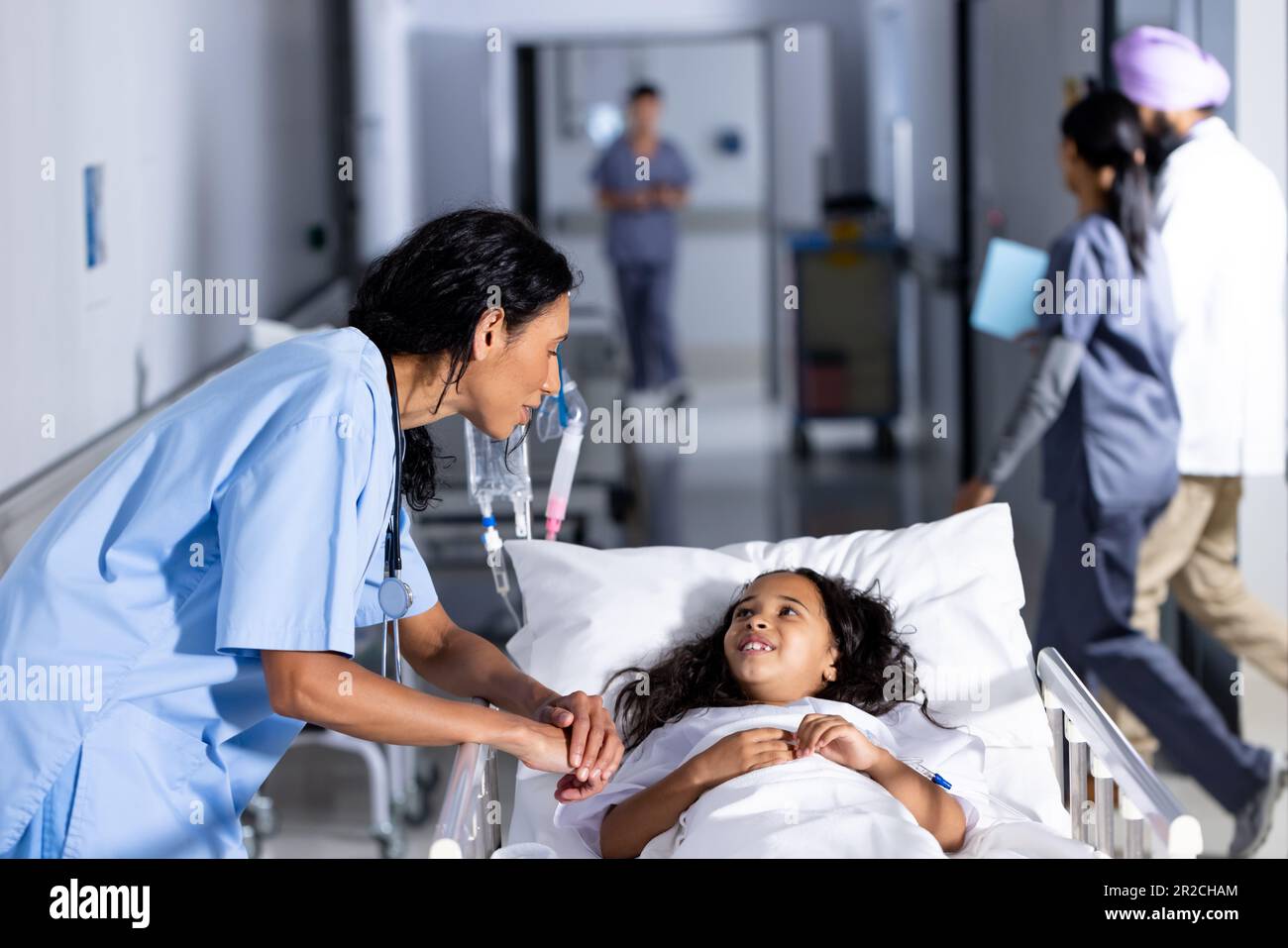 Biracial female doctor and smiling girl patient in bed talking in ...