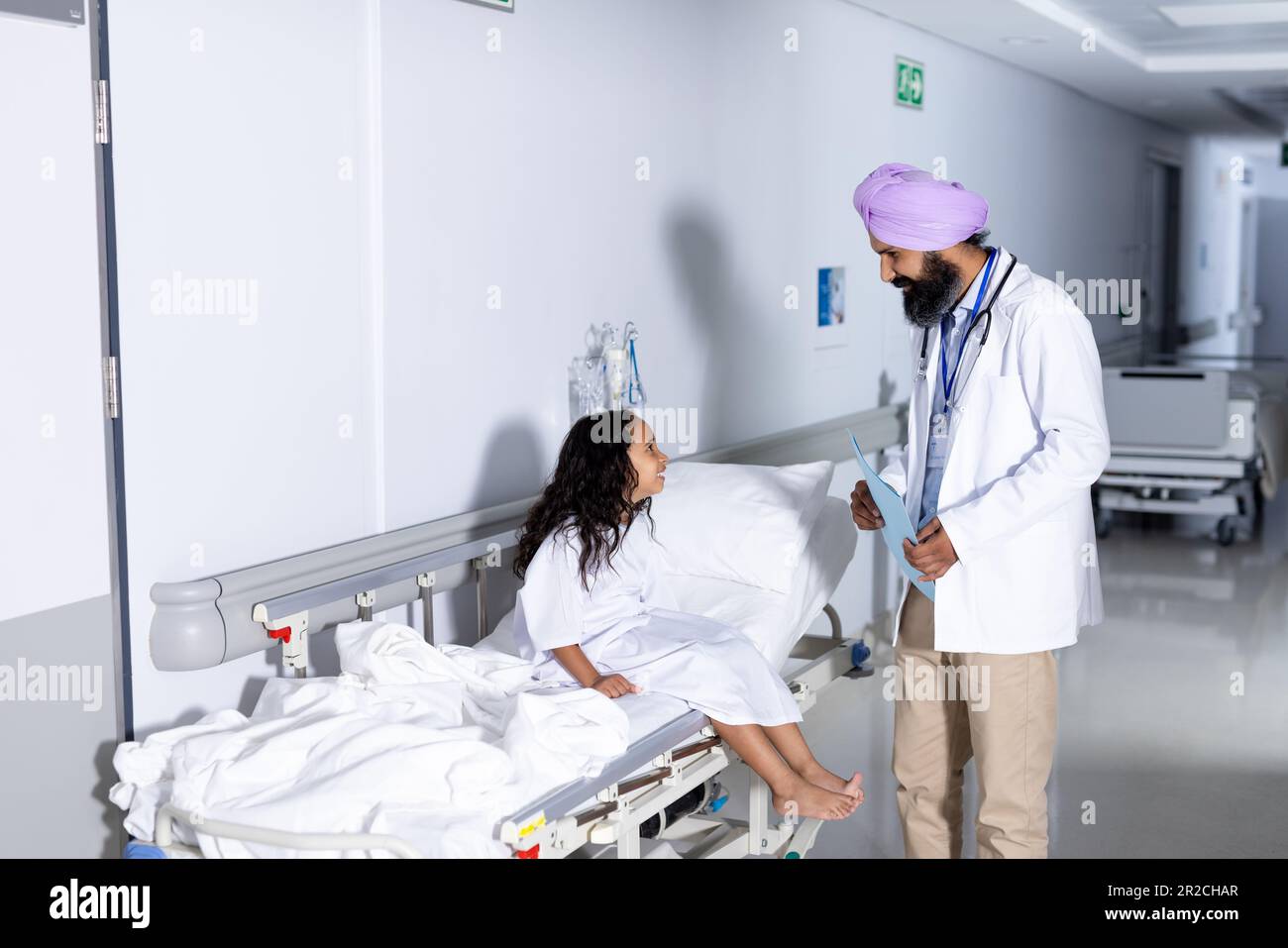 Happy sikh male doctor in turban and biracial girl patient talking in ...