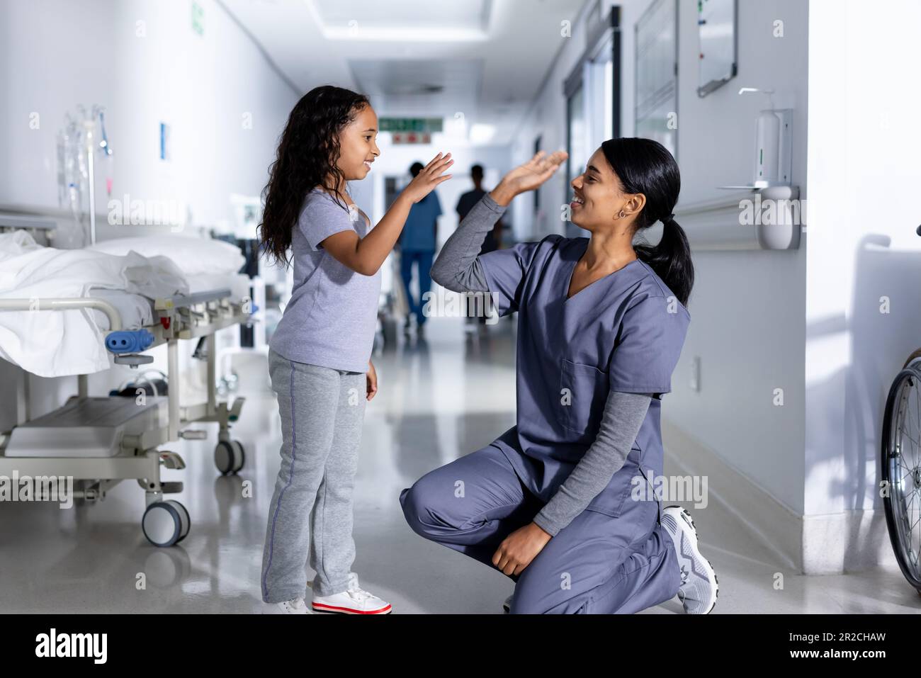 Happy kneeling biracial female doctor and girl patient high fiving in ...