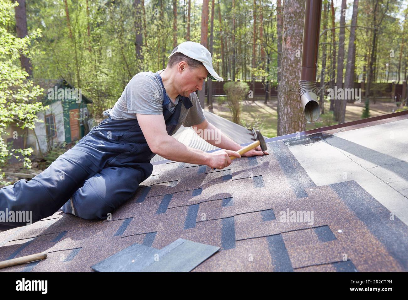 A man mounts soft bitumen shingles with nails and a hammer on the roof ...