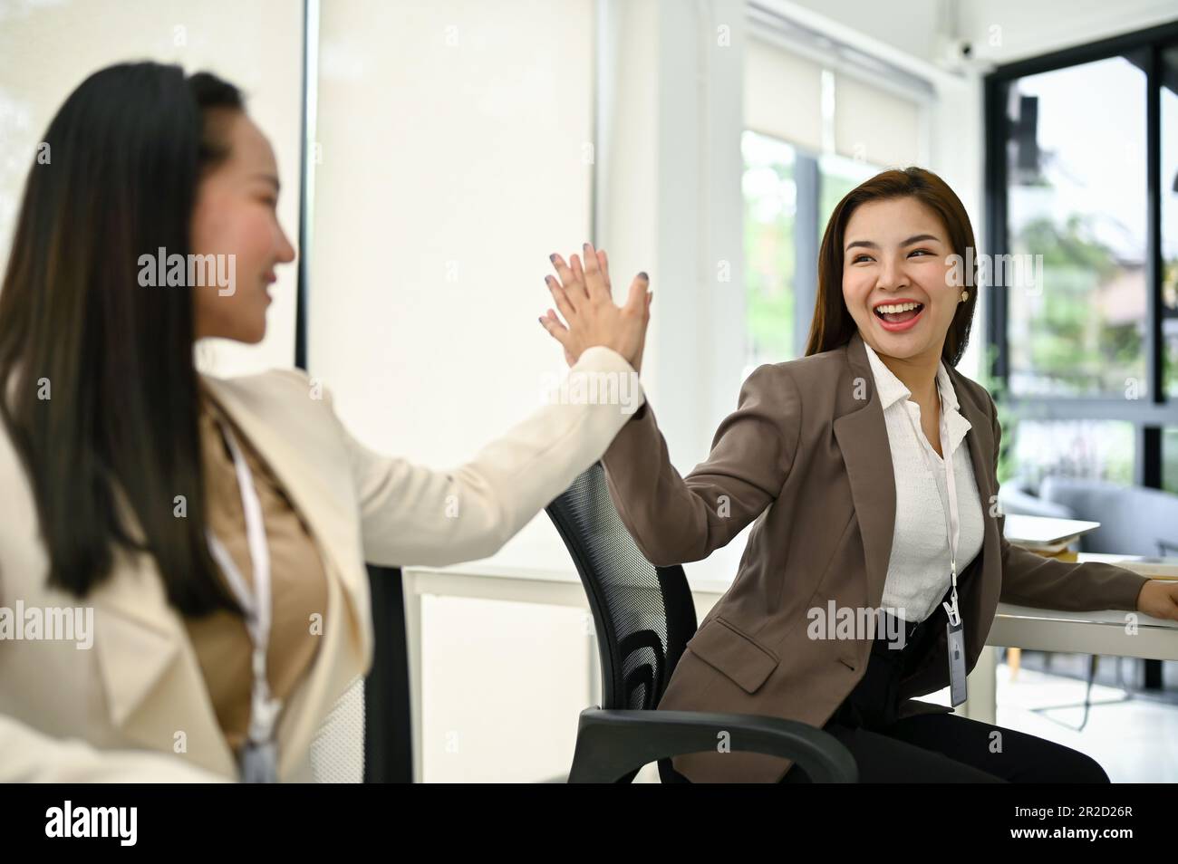 Two joyful and excited young Asian businesswomen giving high fives to ...
