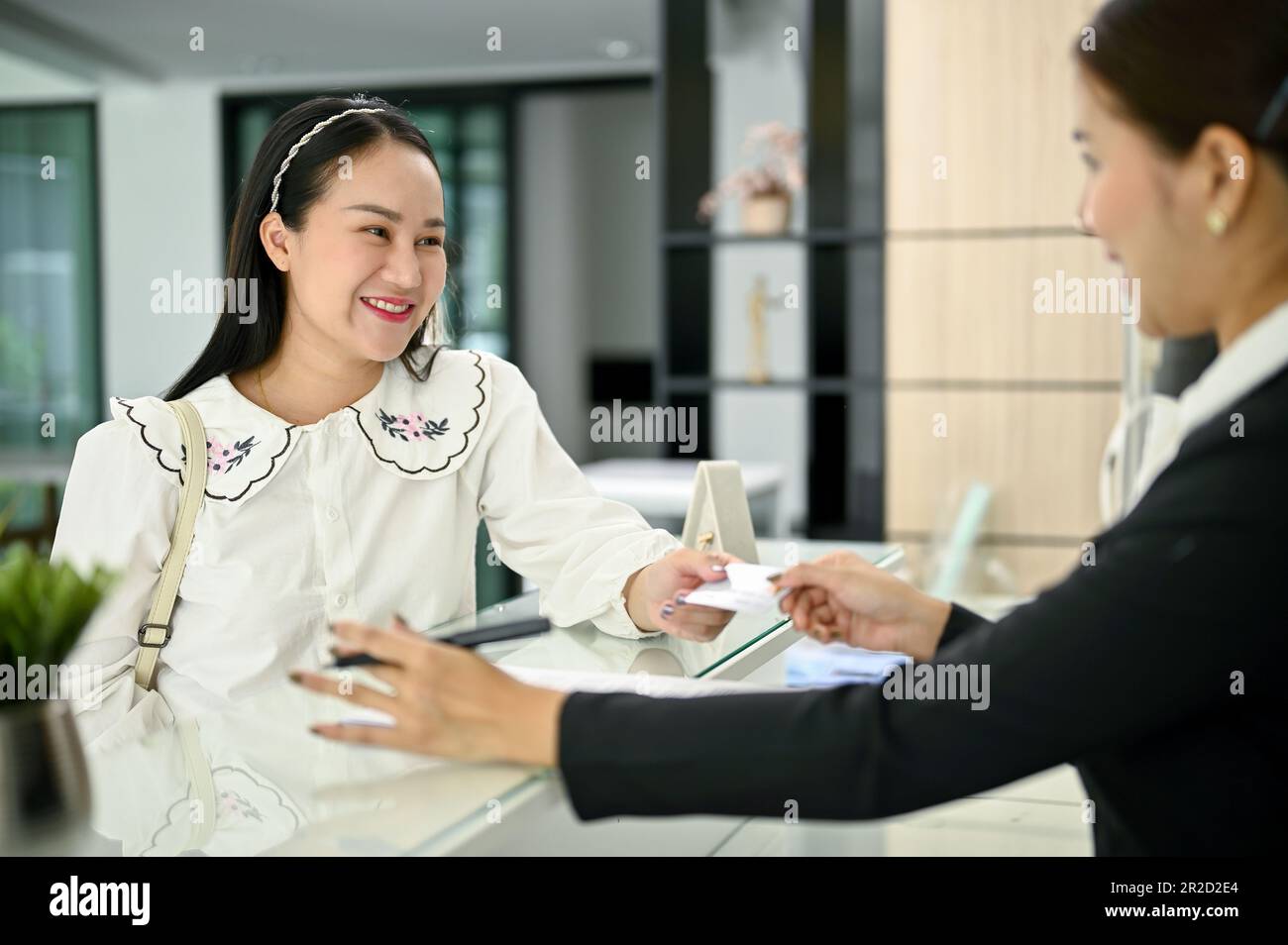 A smiling millennial Asian female customer talking with a receptionist ...