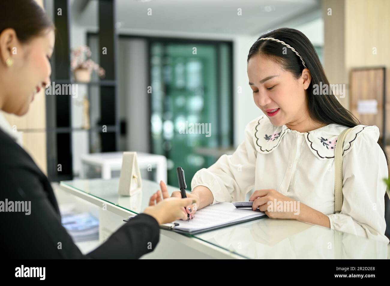 A beautiful Asian female customer filling out a form and signing her ...
