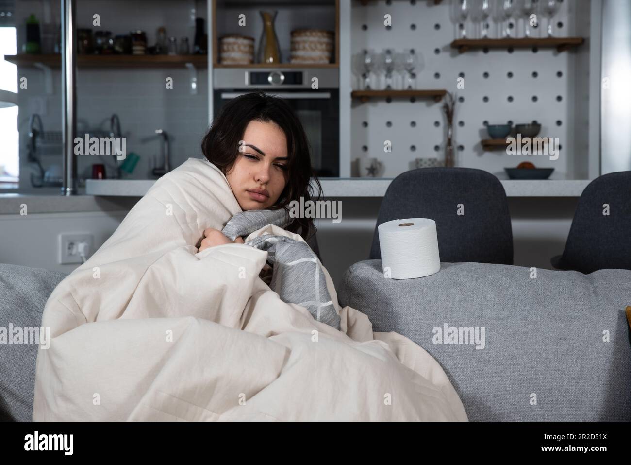 Ill upset young woman sitting on sofa covered with blanket freezing ...