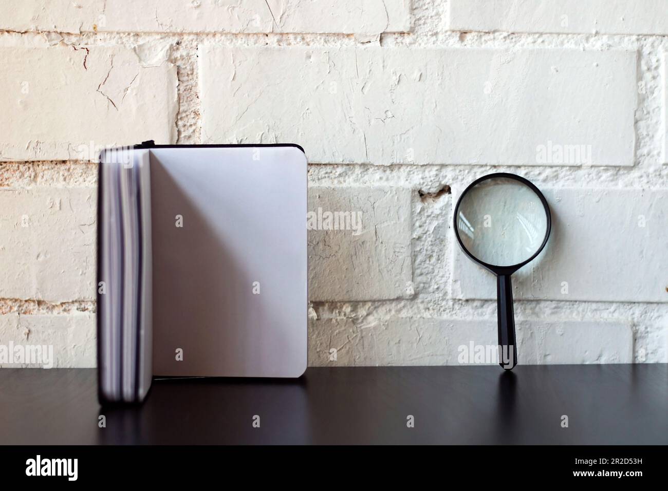 Magnifying glass next to a black notebook Stock Photo - Alamy