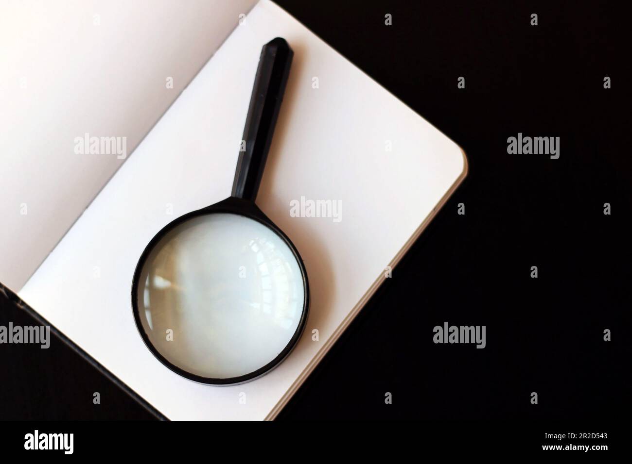 Magnifying glass on top of a black notebook Stock Photo - Alamy