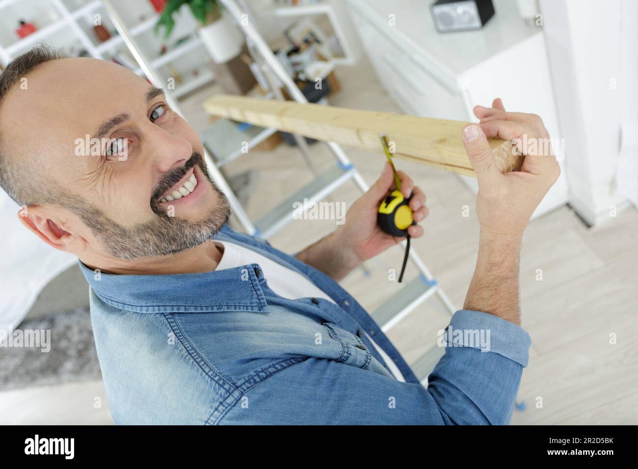 man laughing while measuring wood at home Stock Photo - Alamy
