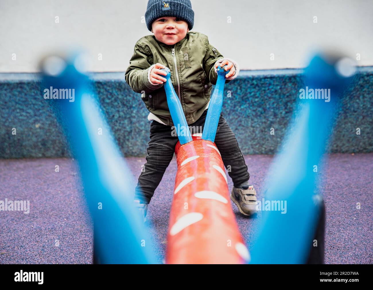 Happy child seen through the handles on a seesaw. Playful kid outdoor ...