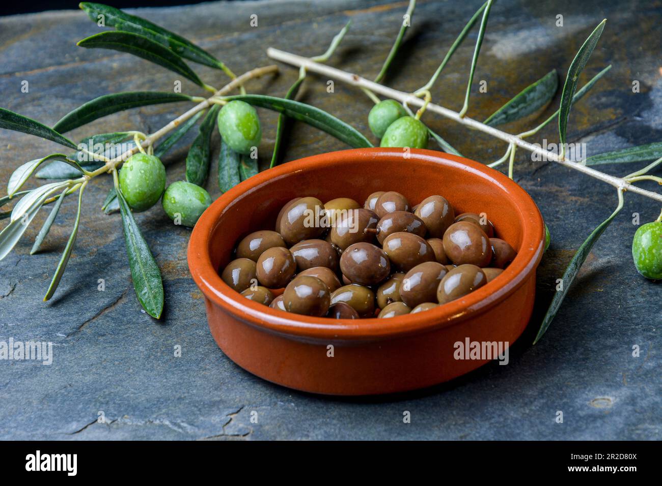 Olives in a clay dish, studio photograph with stone background. Still ...