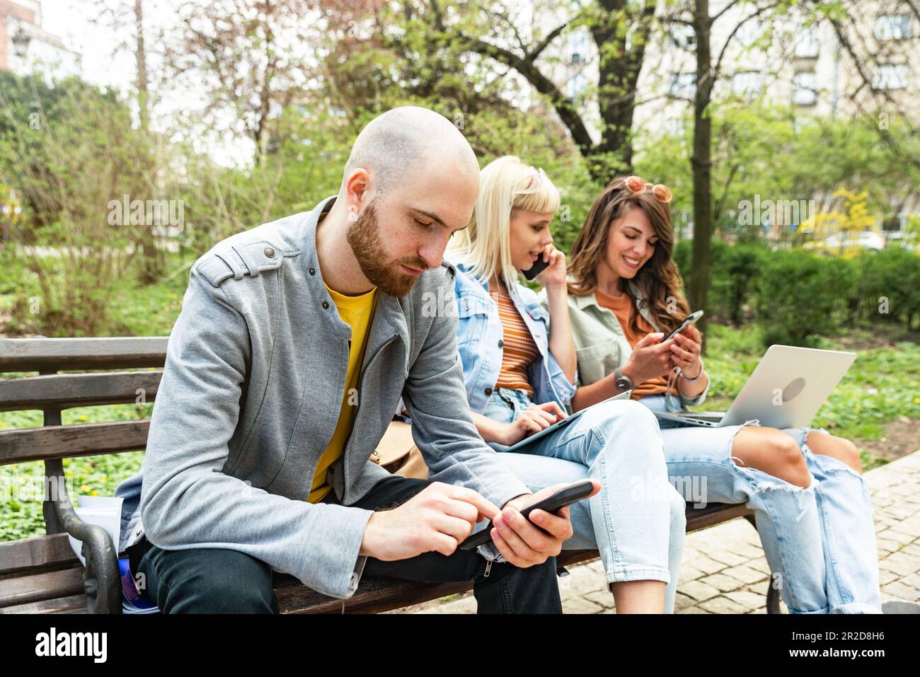 Cheerful classmates university students sitting on a bench in spring ...