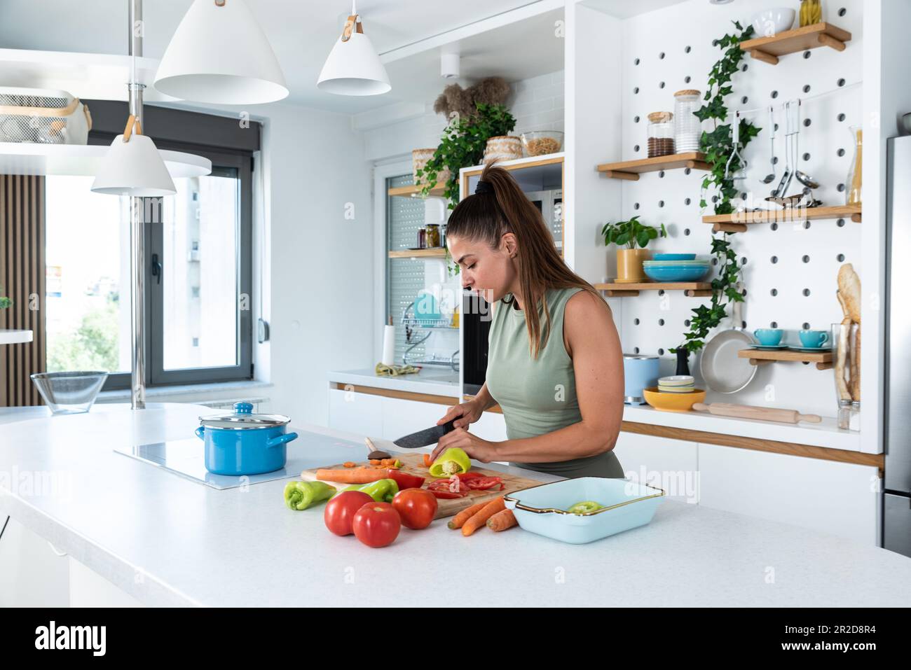 Smiling young sporty woman cooking salad, cutting fresh vegetables in ...