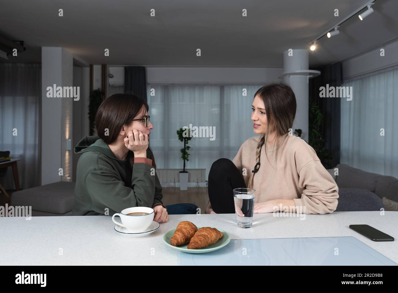 Two millennial girl friends at home talking, drinking coffee ...