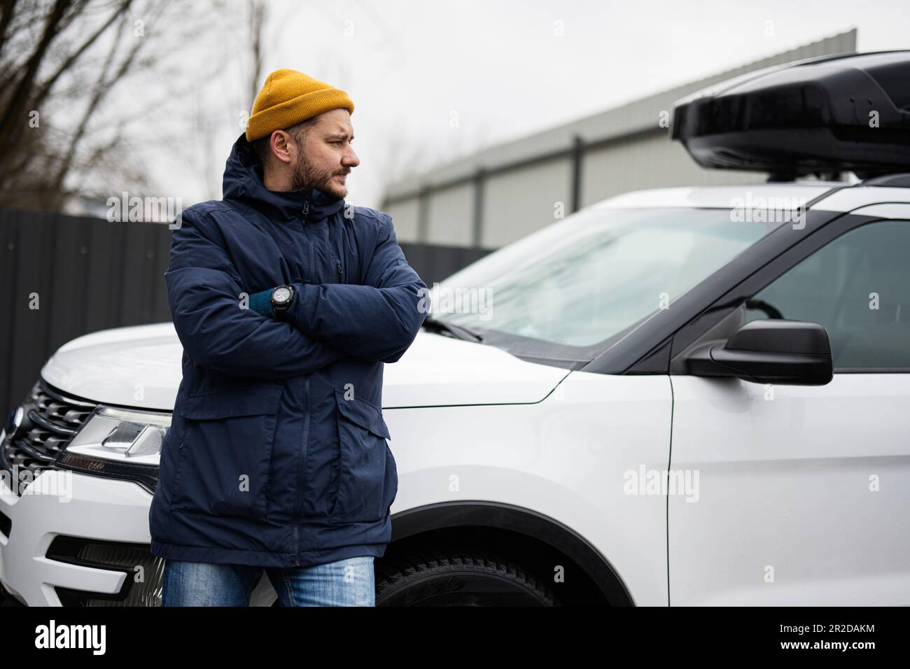 Man driver wear jacket and yellow hat against his american SUV car with ...