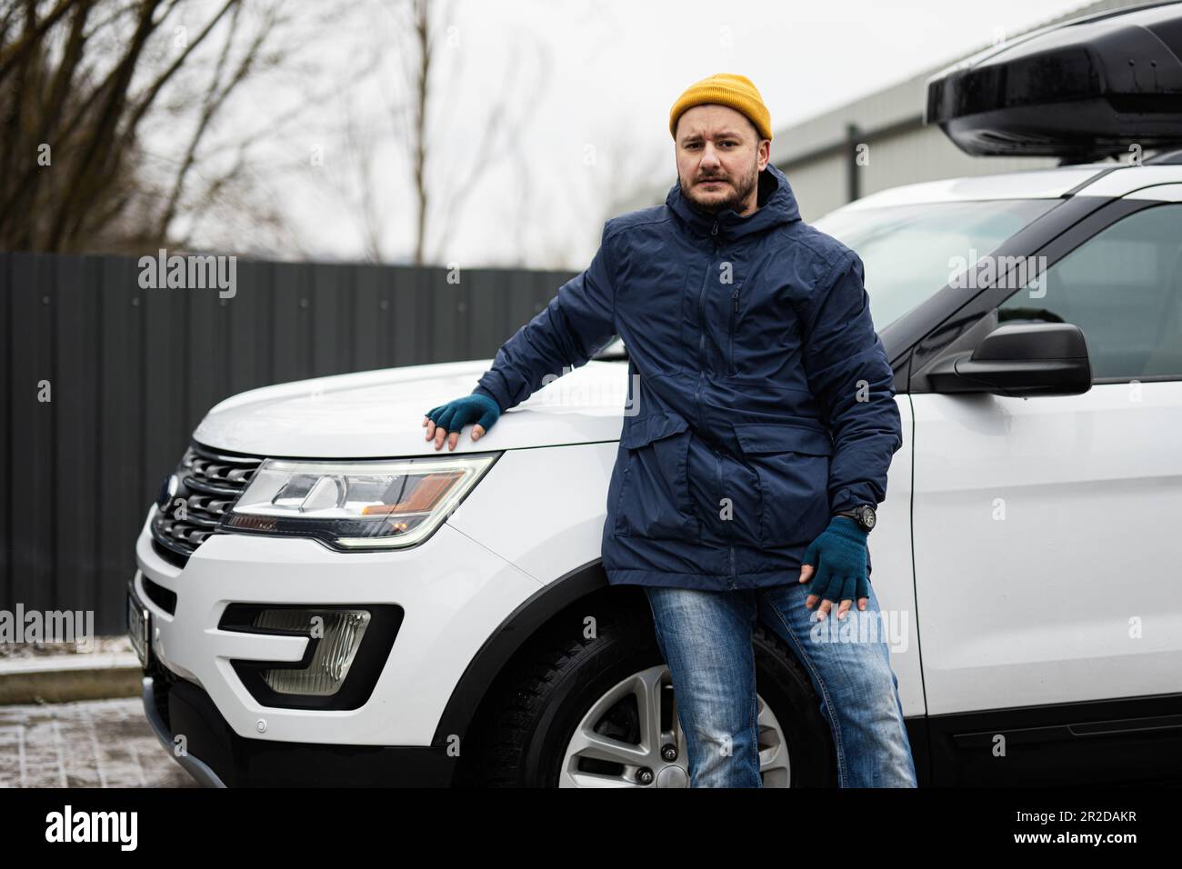 Man driver wear jacket and yellow hat against his american SUV car with ...