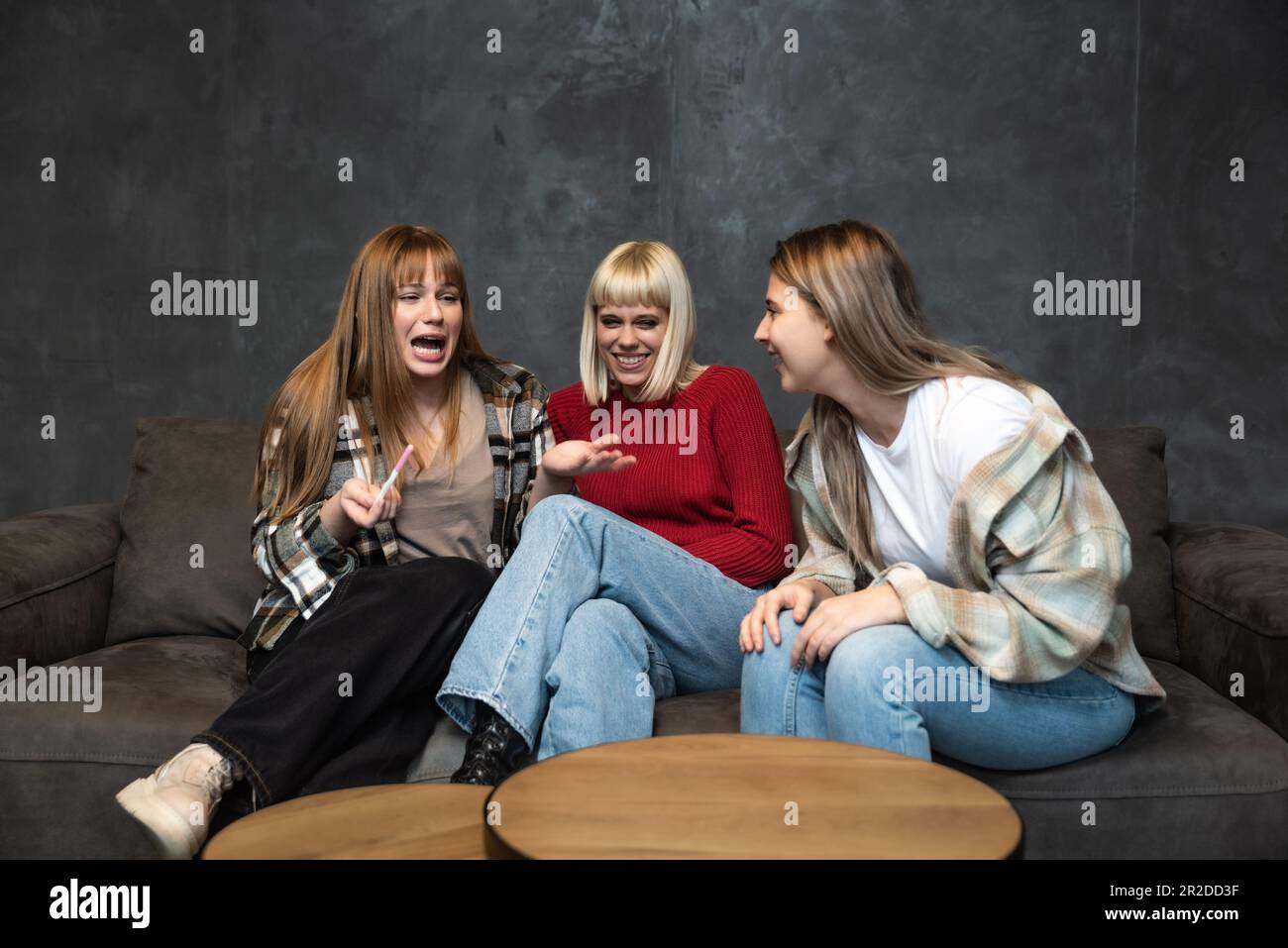 Three young happy female friends, college roommates sitting on the sofa ...