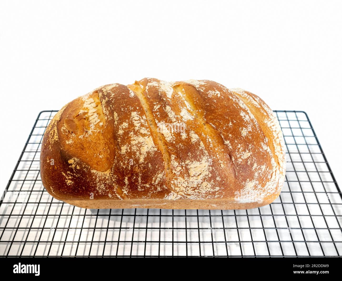 Newly baked loaf cooling on a metal mesh tray on a white background ...