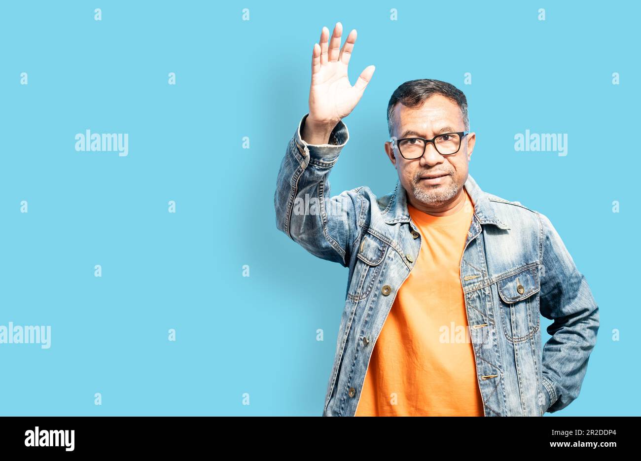 A man waving his hand, wearing blue jeans and an orange t-shirt and ...