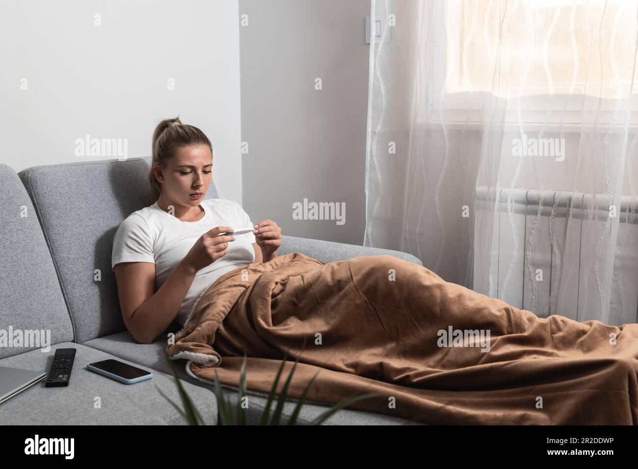 Young sick stressed woman lying at home covered with blanket checking ...