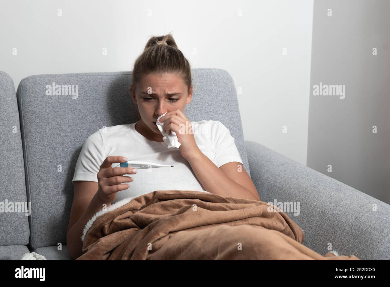 Young sick stressed woman lying at home covered with blanket checking ...