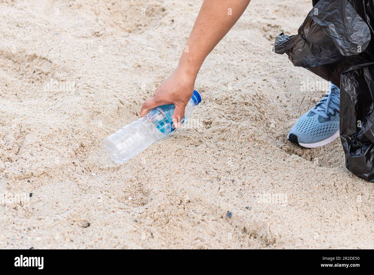Woman cleans up by picking up plastic bottles at the beach. Concept of ...