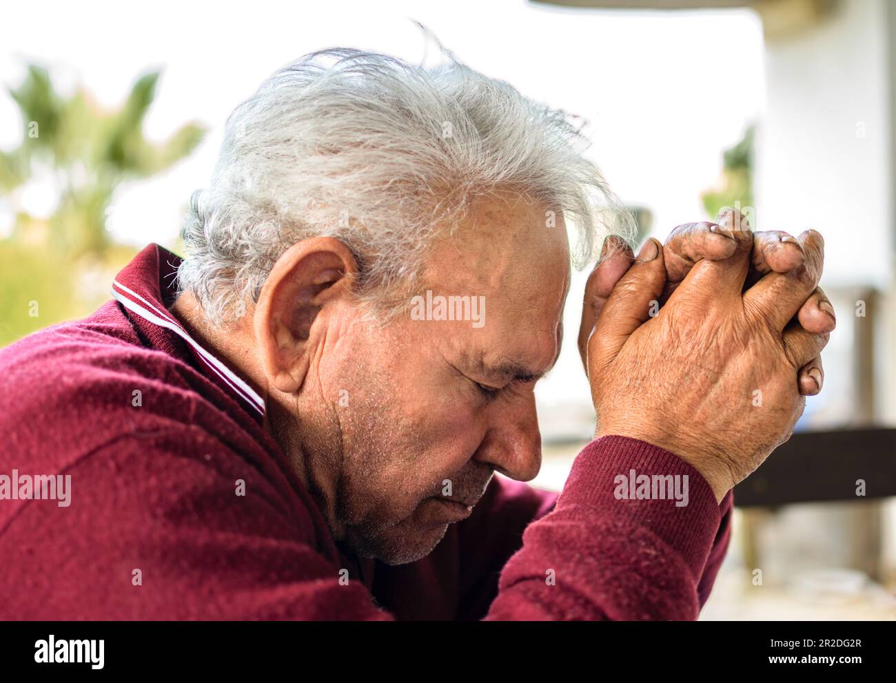 Old man with red sweater and gray hair praying with his hands in ...