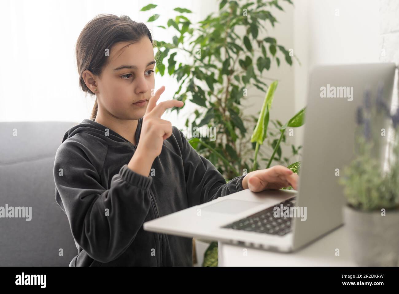 A teenage girl sits in front of her laptop learning sign language, a ...