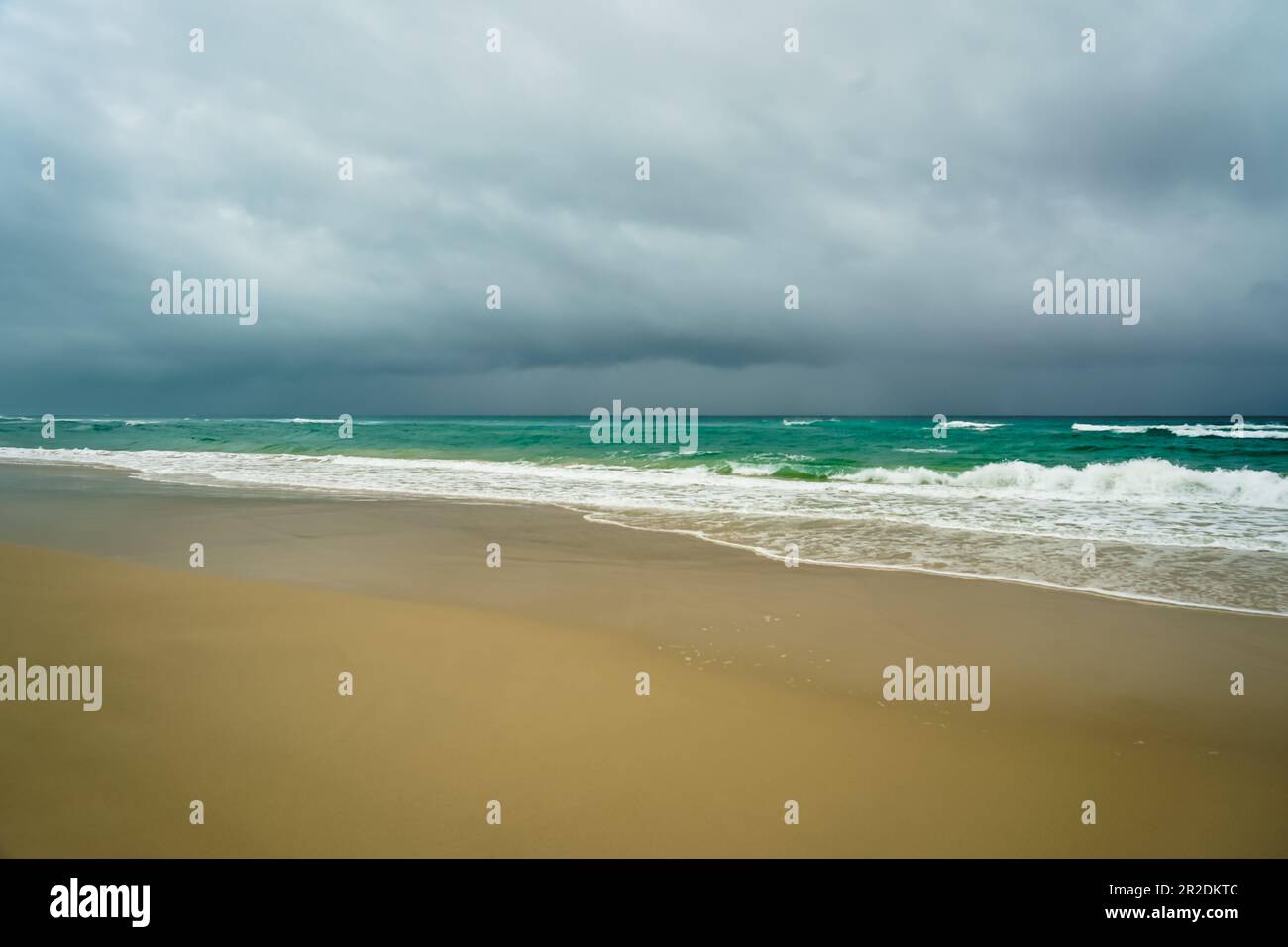 Rain clouds over the ocean, with surf waves breaking on a sandy beach ...