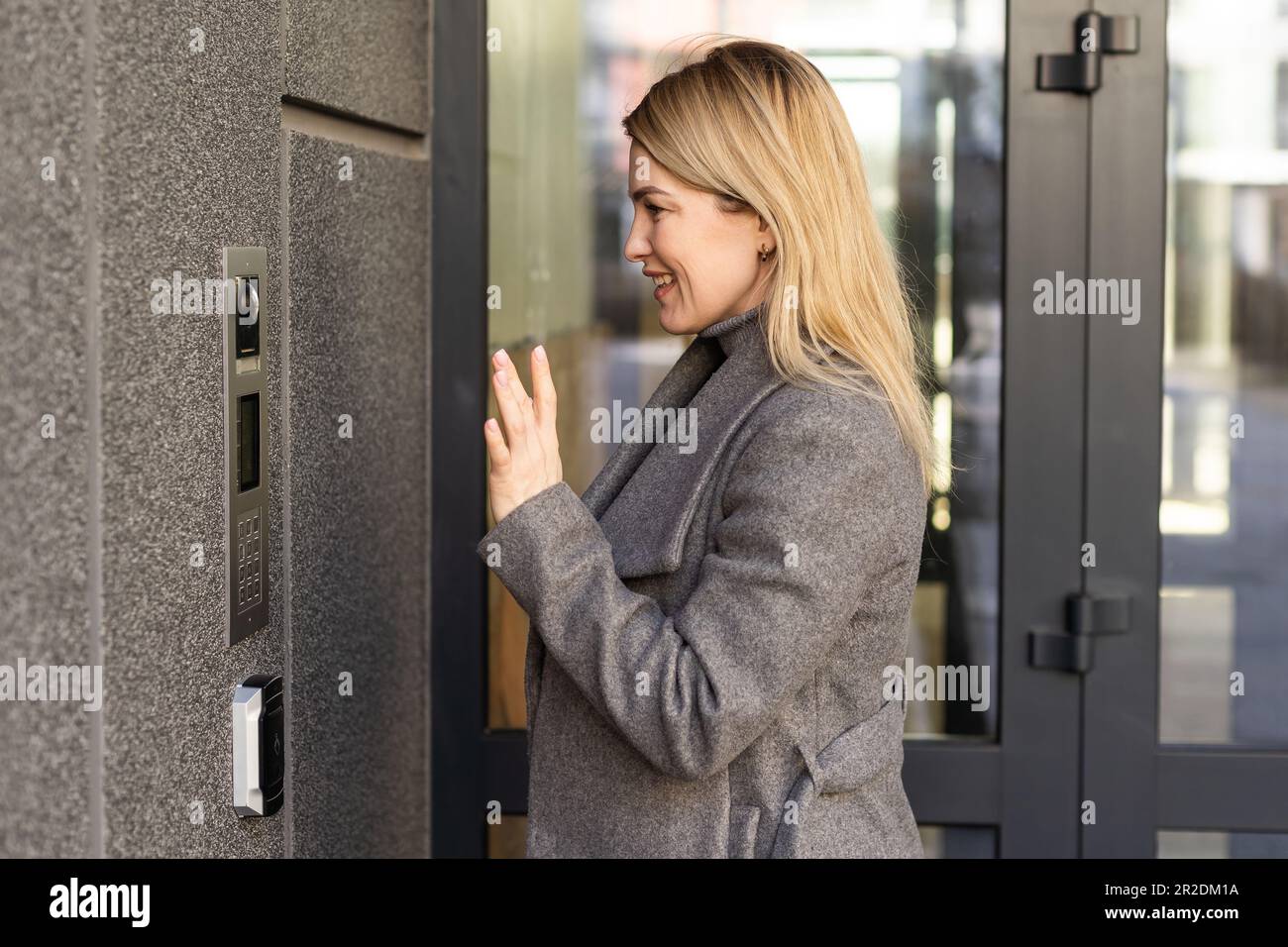 Happy woman ringing on doorbell at building entrance. Using intercom ...