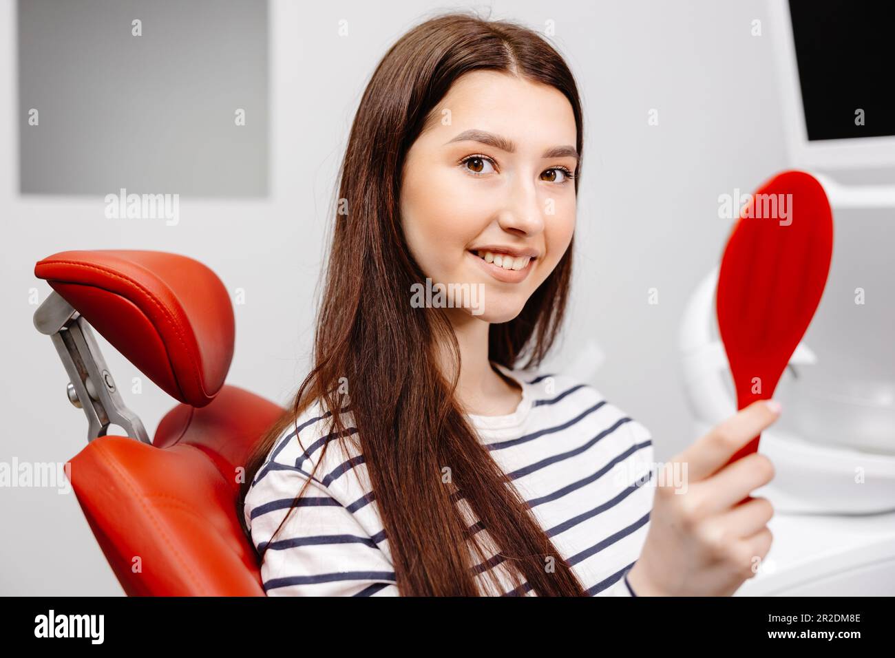 Happy caucasian female patient looking at mirror after dental treatment in clinic. Cheerful ...