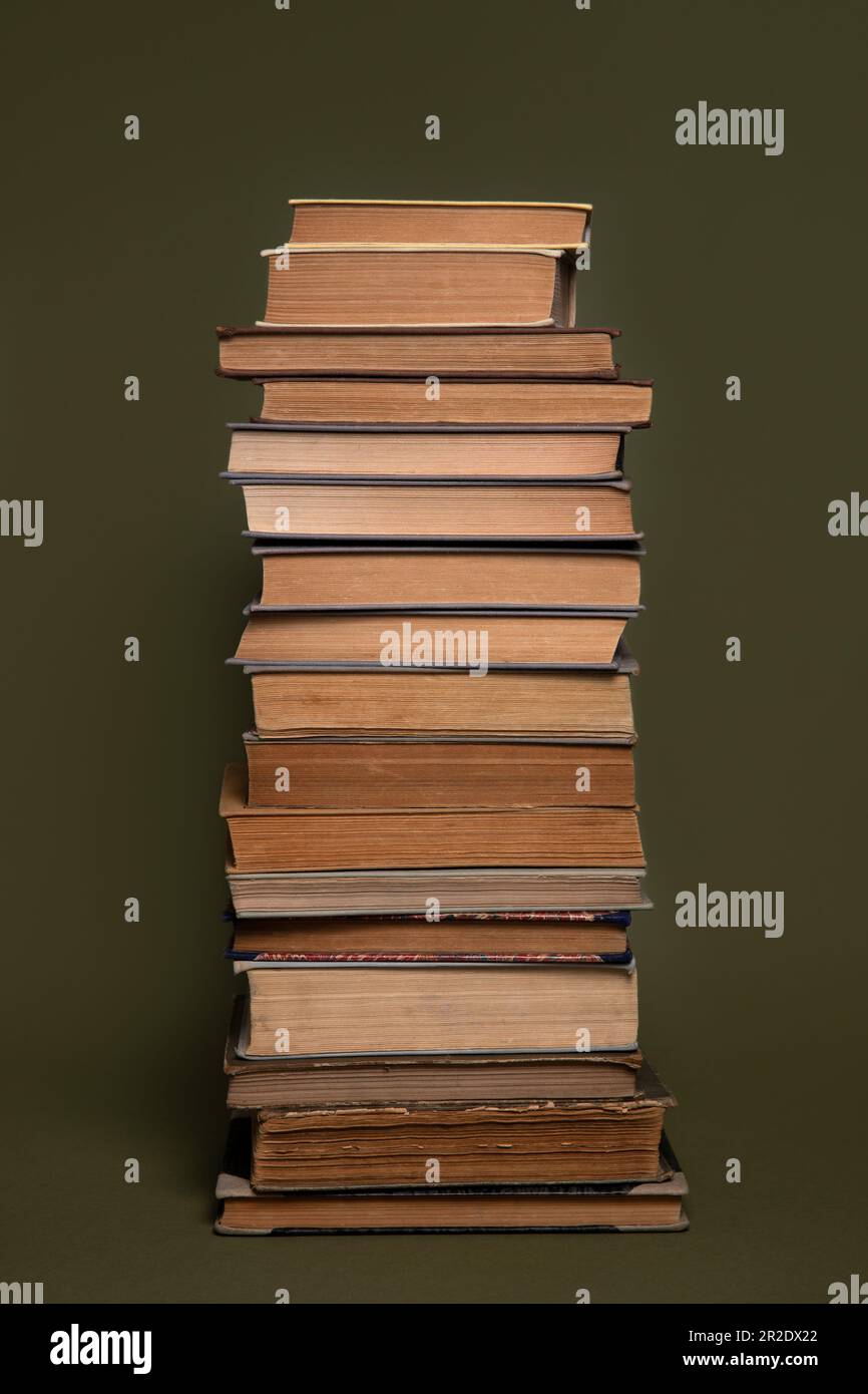 A tall tower of old books that have yellowed pages, against an olive ...