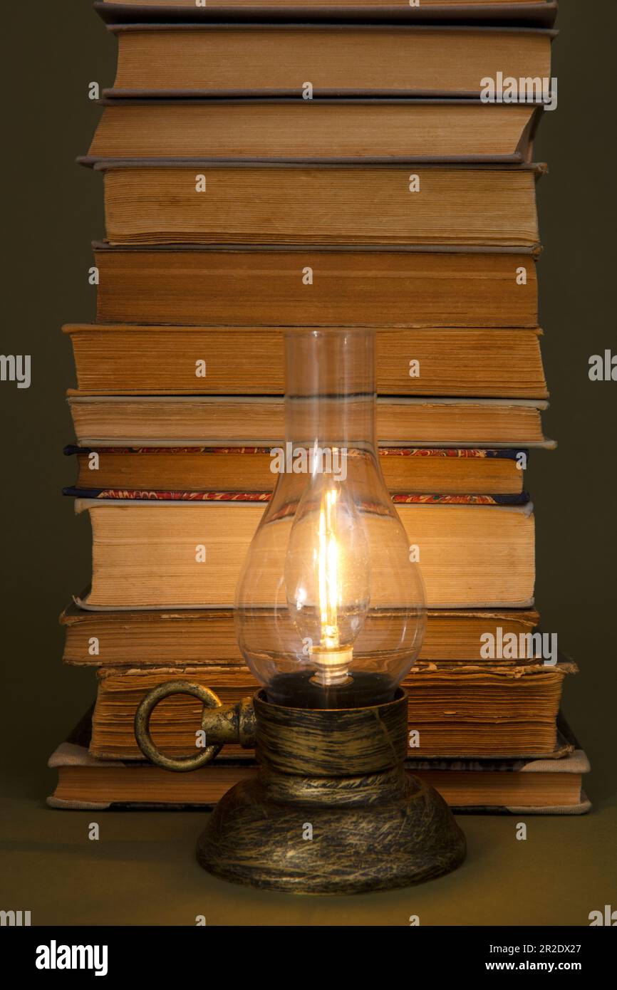 Old books and a lamp with a burning light on an olive background ...