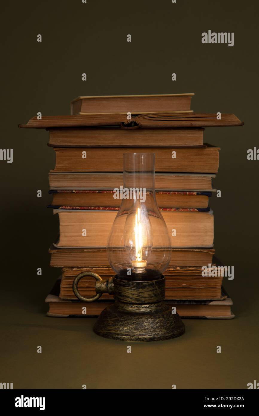 Old books and a lamp with a burning light on an olive background ...