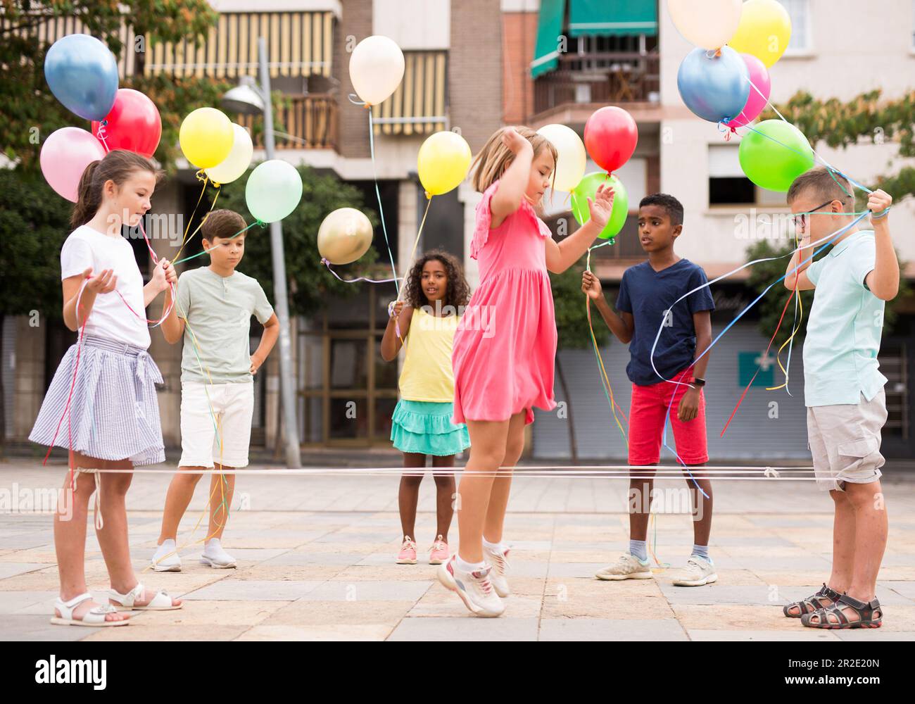 Happy tweenagers with balloons playing chinese jump rope in yard Stock ...